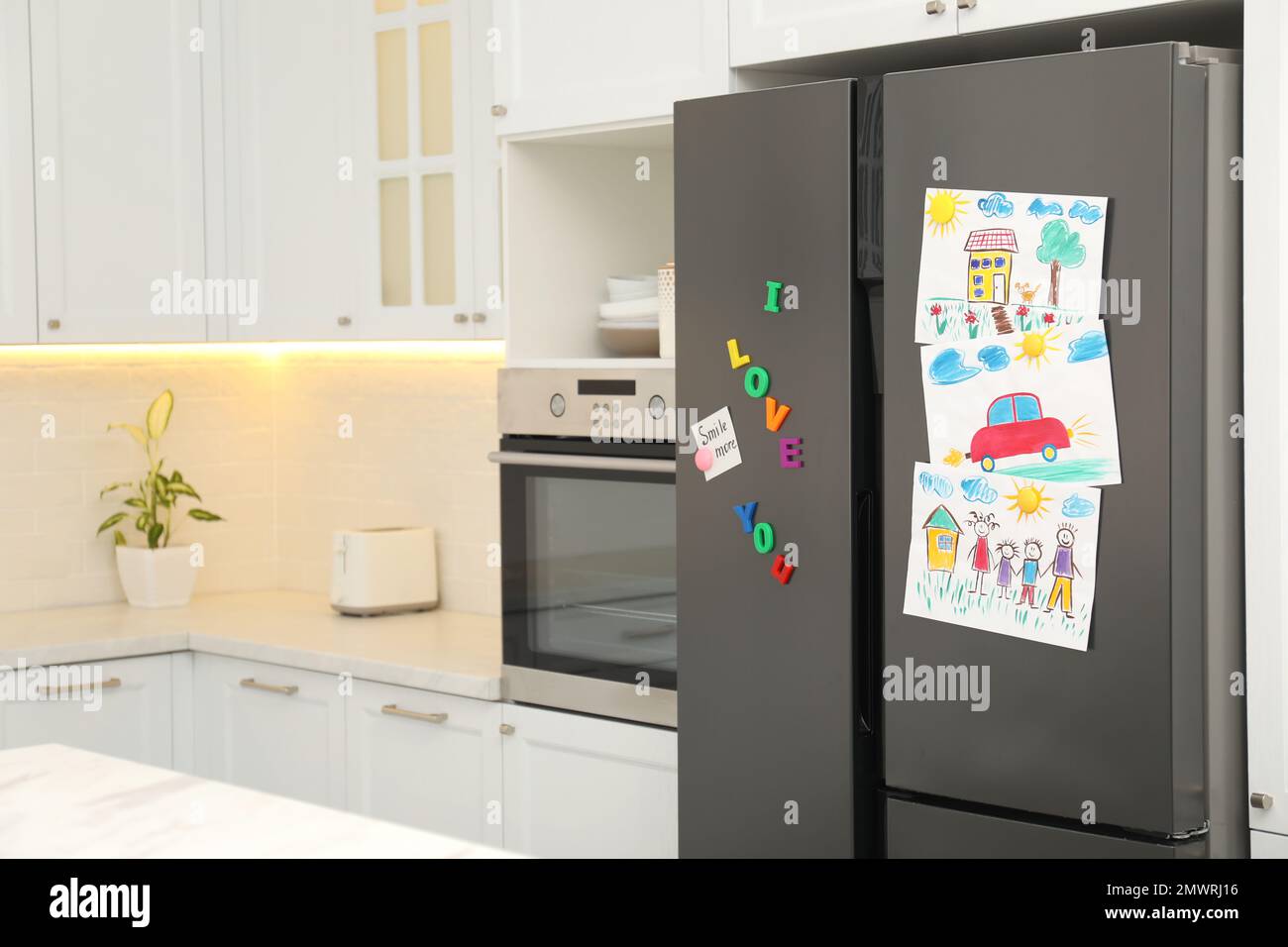 Modern refrigerator with child's drawings, note and magnets in kitchen ...