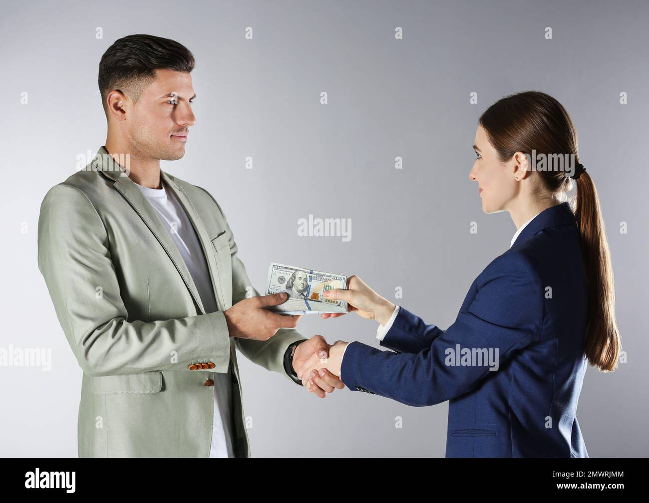 Woman shaking hands with man and offering bribe on grey background ...