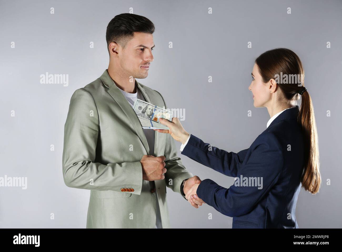 Woman shaking hands with man and offering bribe on grey background ...