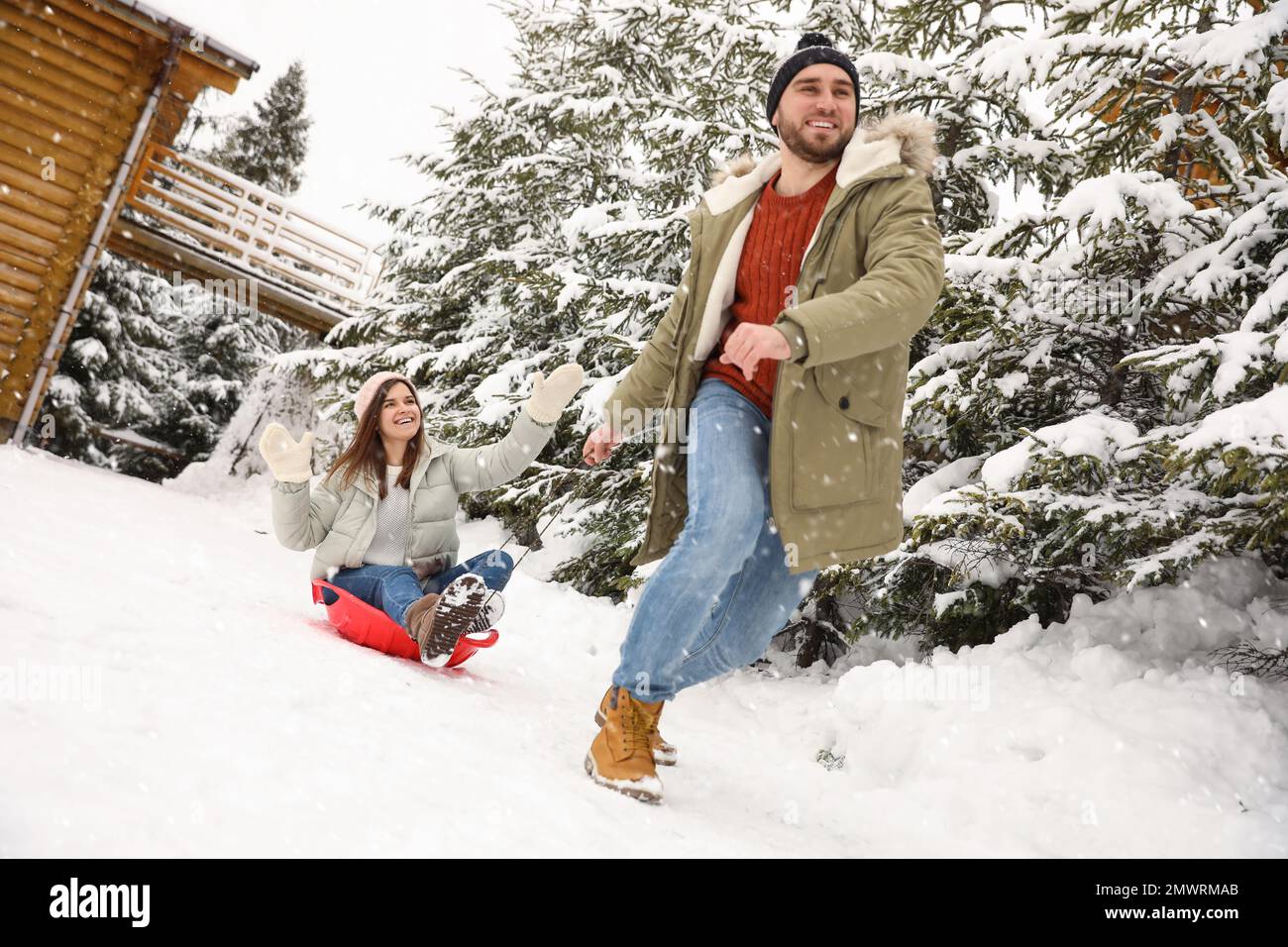 Young man pulling sled with his girlfriend outdoors on snowy day ...