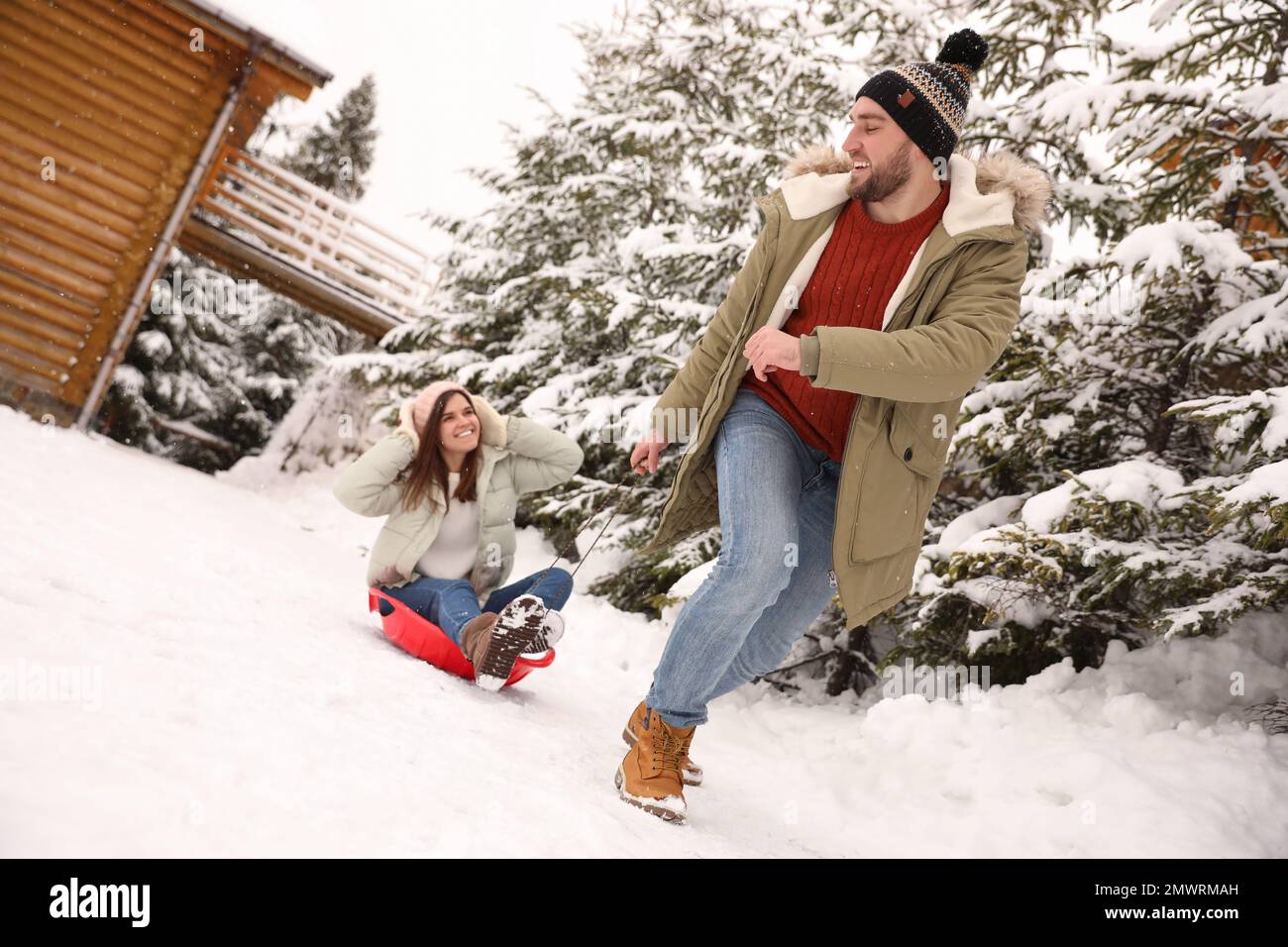 Young man pulling sled with his girlfriend outdoors on snowy day ...