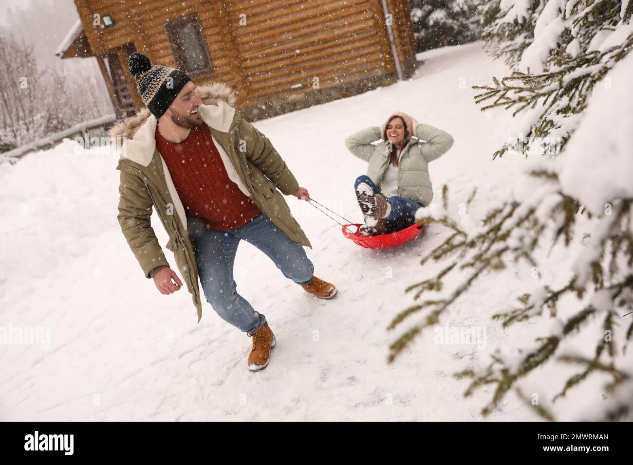 Young man pulling sled with his girlfriend outdoors on snowy day ...