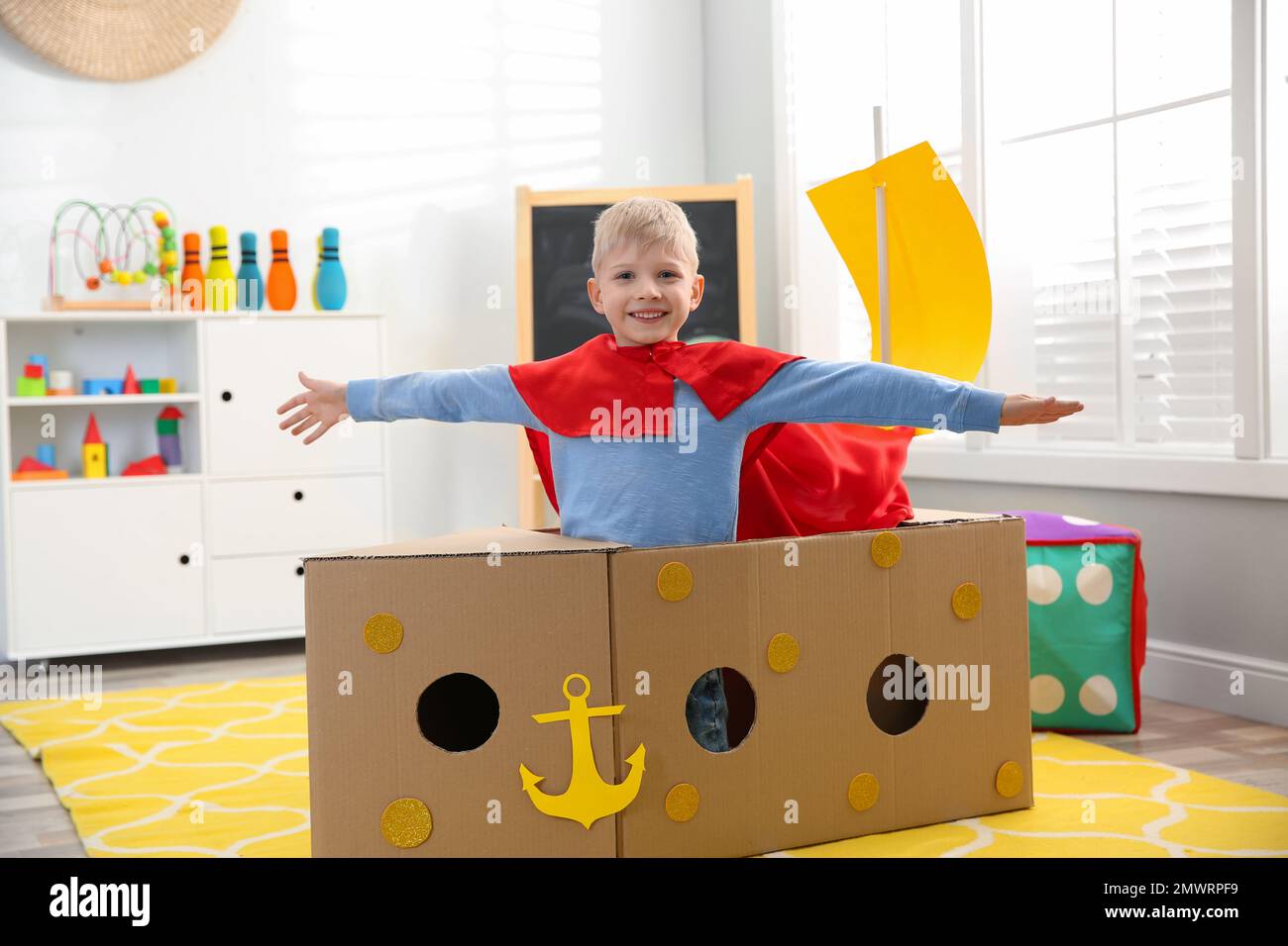 Little child in red cape playing with ship made of cardboard box at ...