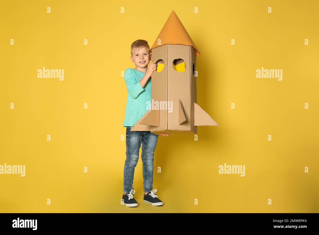 Little child playing with rocket made of cardboard box on yellow ...
