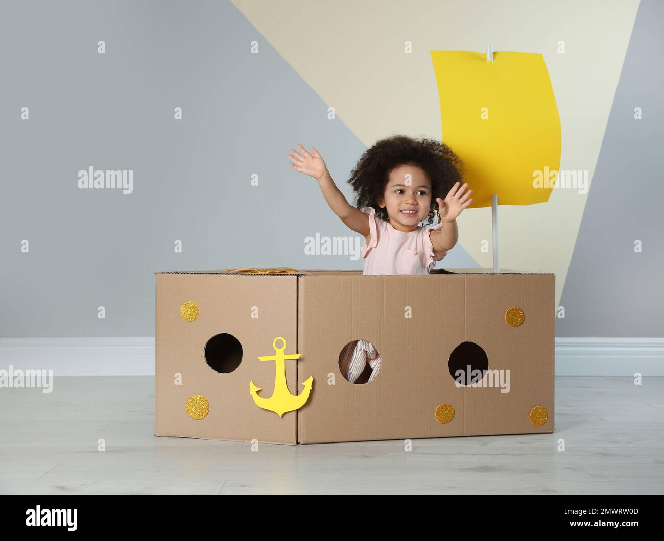 Cute African American child playing with cardboard ship near color wall ...