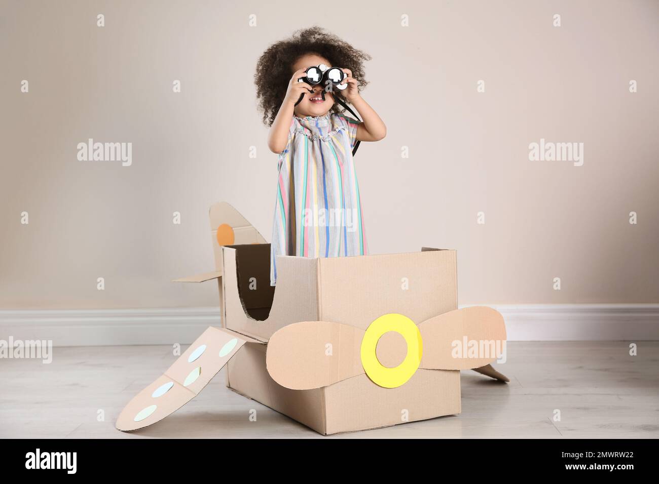 Cute African American child playing with cardboard plane and binoculars ...