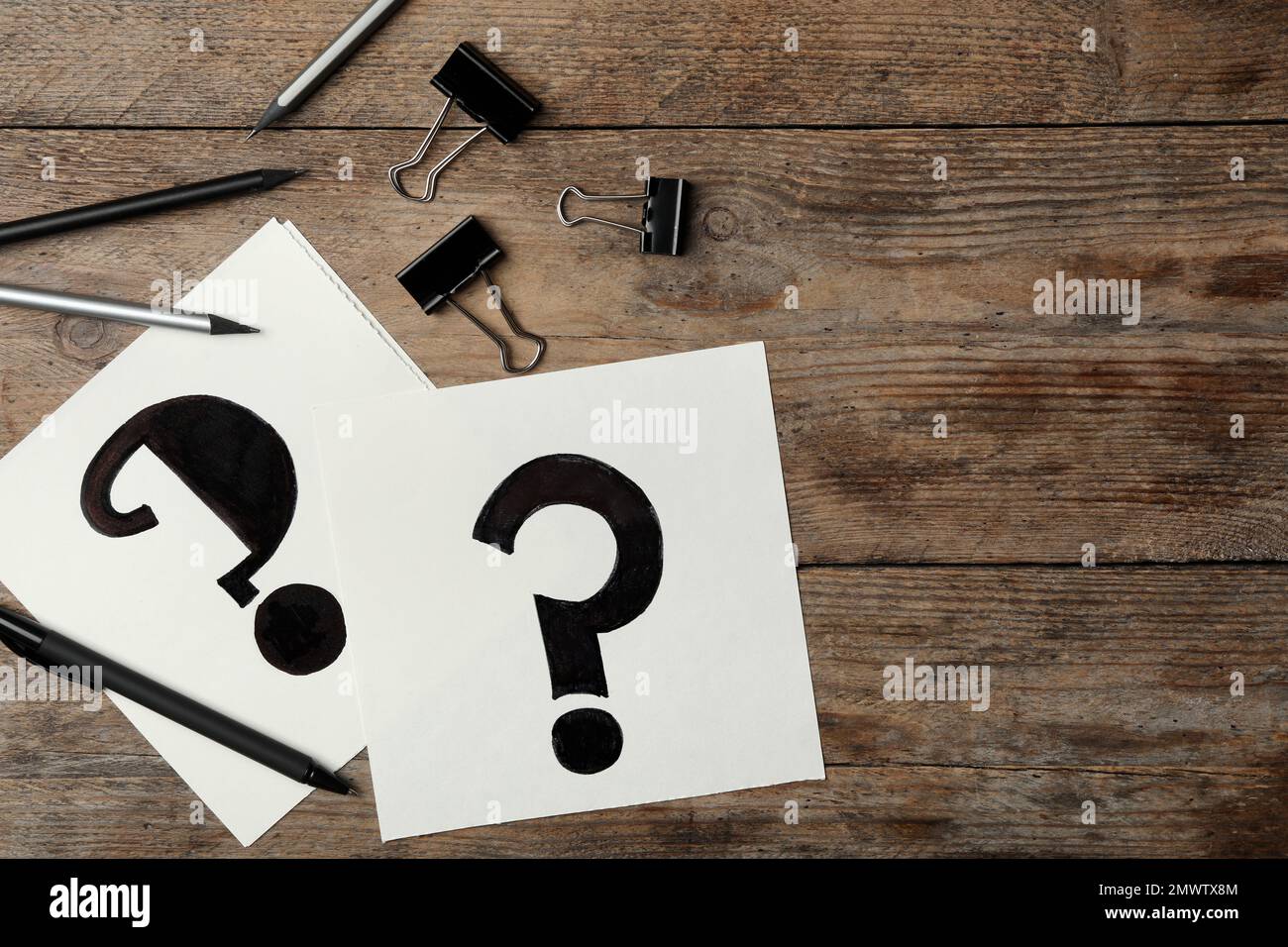 Sheets of paper with question marks and stationery on wooden table ...