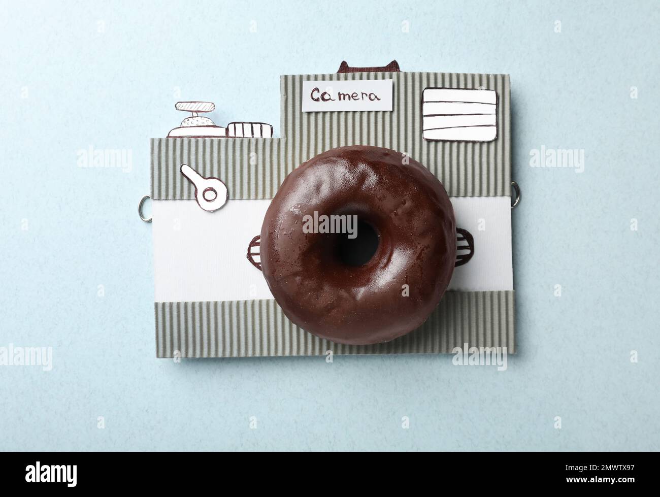 Camera made from donut and piece of cardboard on light blue background ...