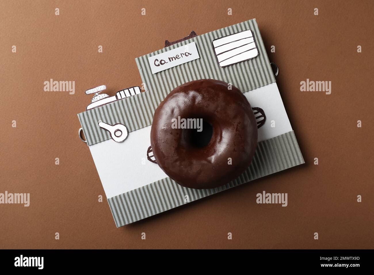 Camera made from donut and piece of cardboard on brown background, top ...