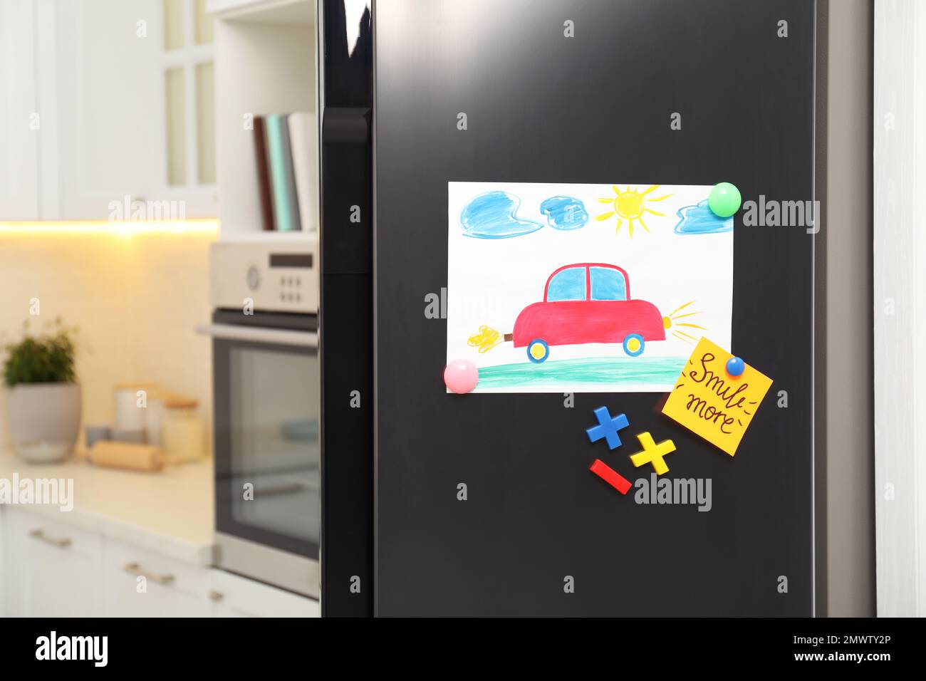 Modern refrigerator with child's drawing, note and magnets in kitchen ...