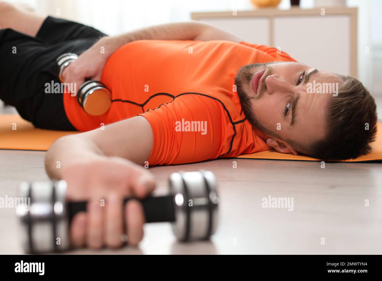 Lazy young man with sport equipment on yoga mat at home Stock Photo - Alamy