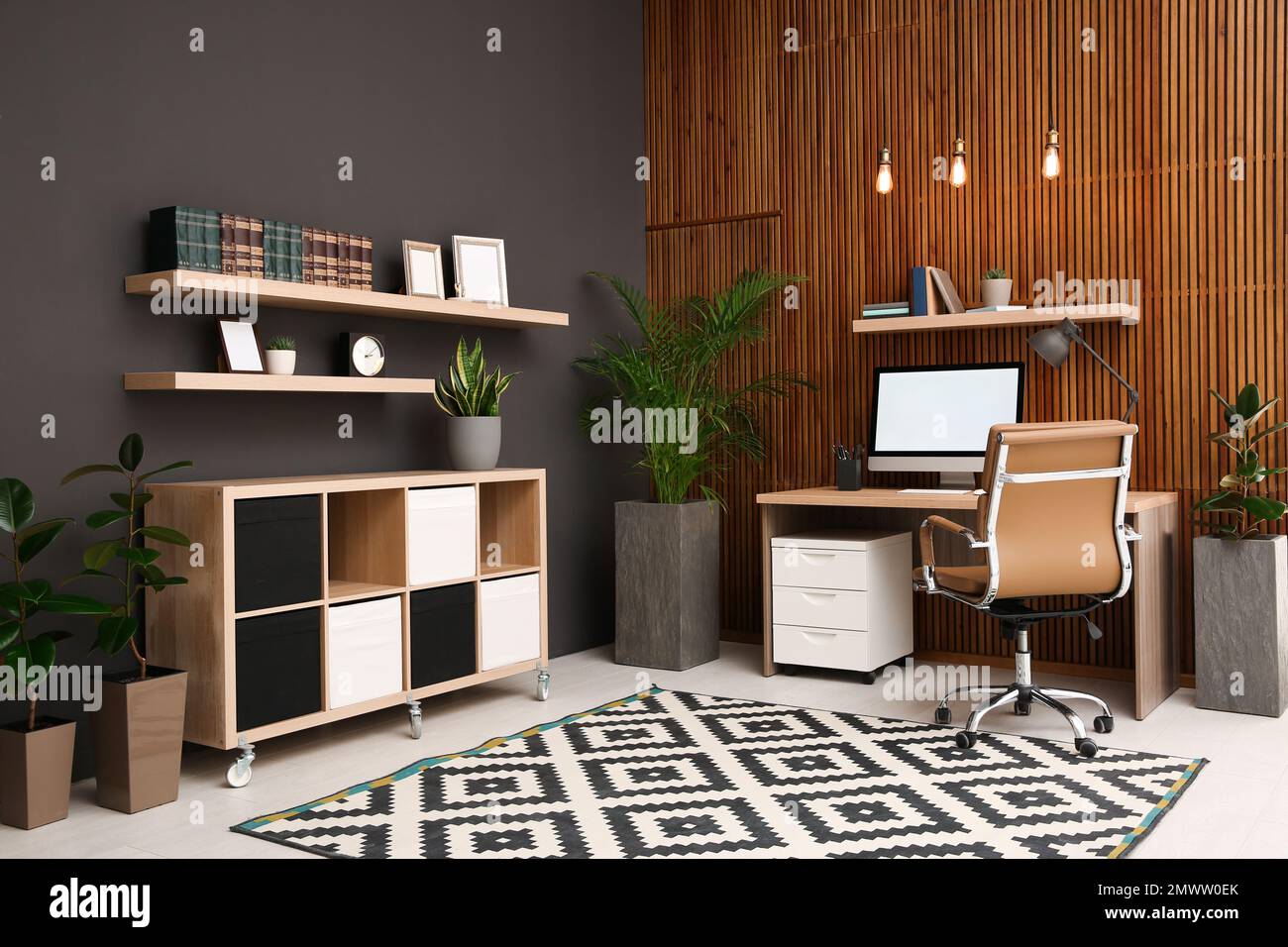 Comfortable workplace with computer near wooden wall in stylish room ...