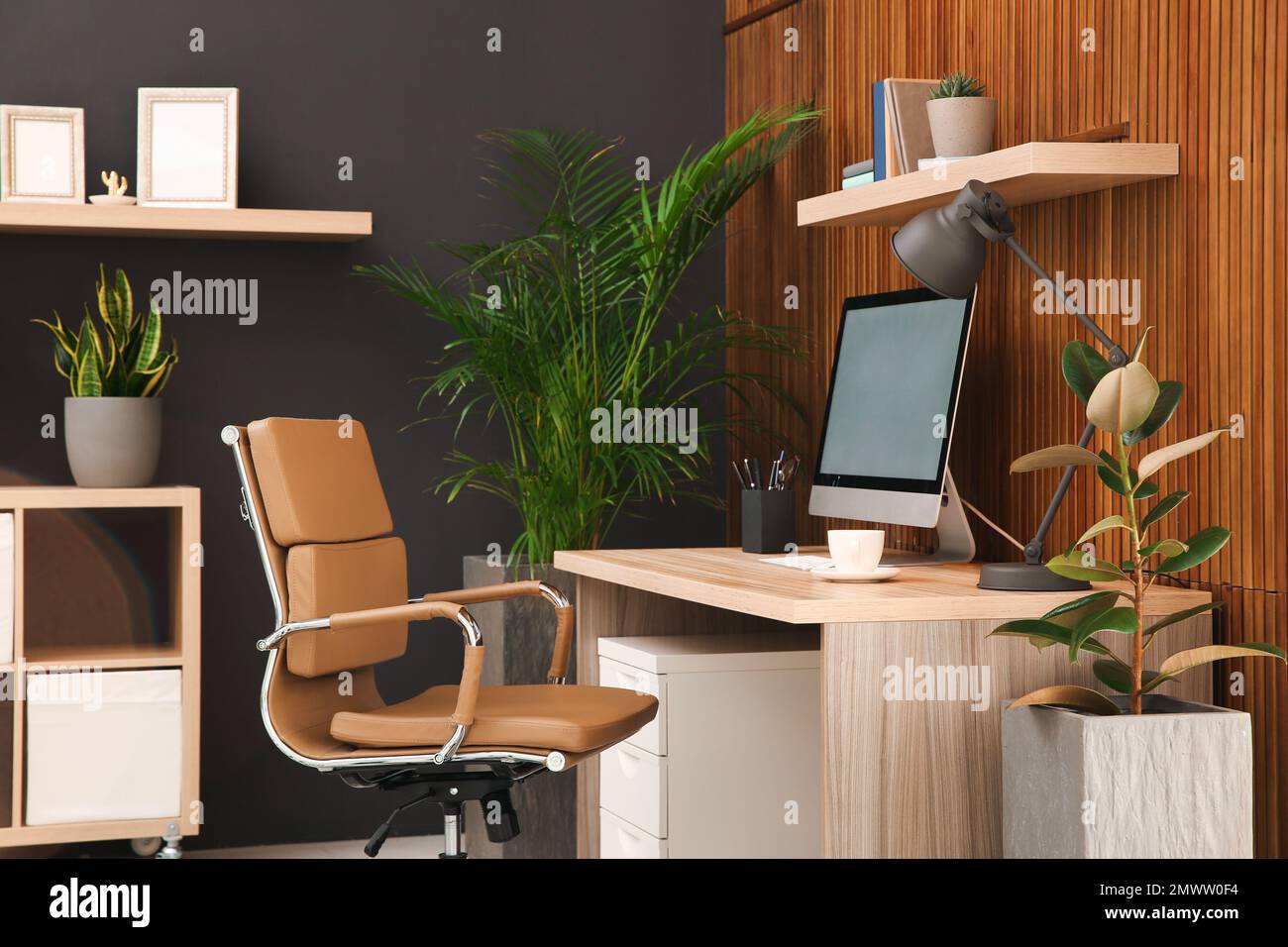 Comfortable workplace with computer near wooden wall in stylish room ...