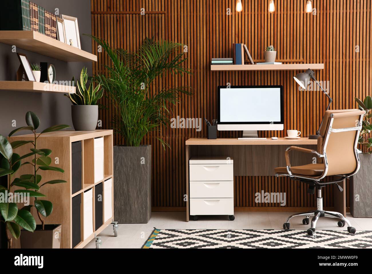 Comfortable workplace with computer near wooden wall in stylish room ...