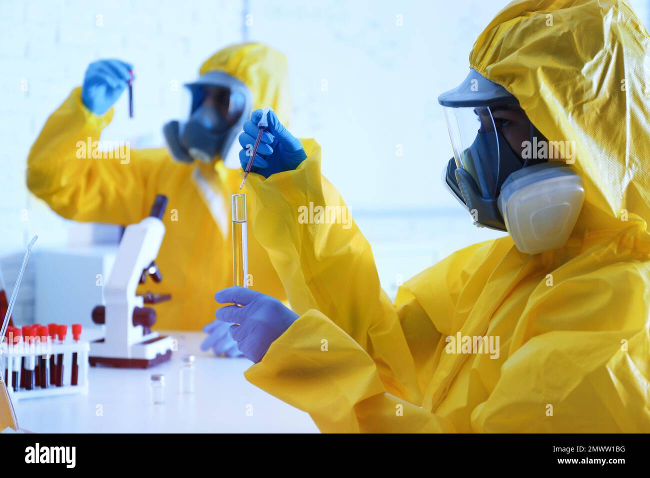 Scientist in chemical protective suit dripping blood into test tube at ...