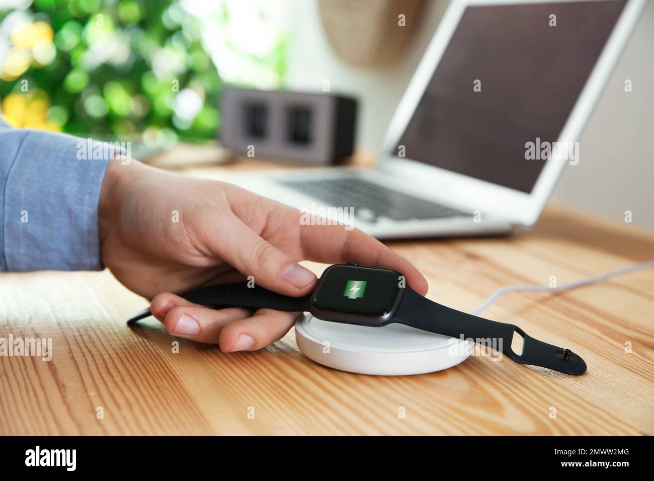 Man putting smartwatch onto wireless charger at wooden table, closeup ...