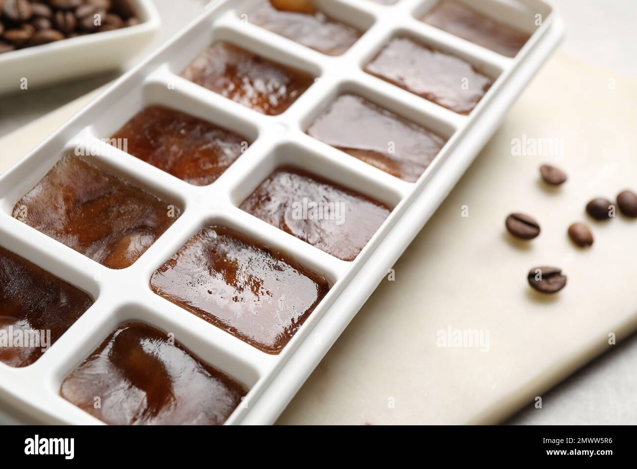 Ice cubes in tray and coffee beans on grey table, closeup Stock Photo ...
