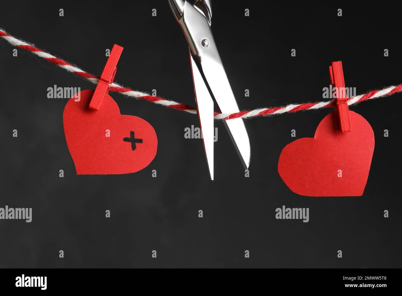 Red paper hearts on rope and scissors against black background ...