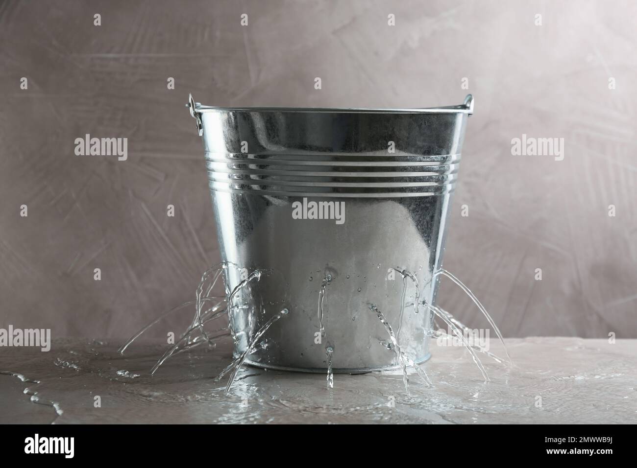 Leaky bucket with water on table against grey background Stock Photo ...