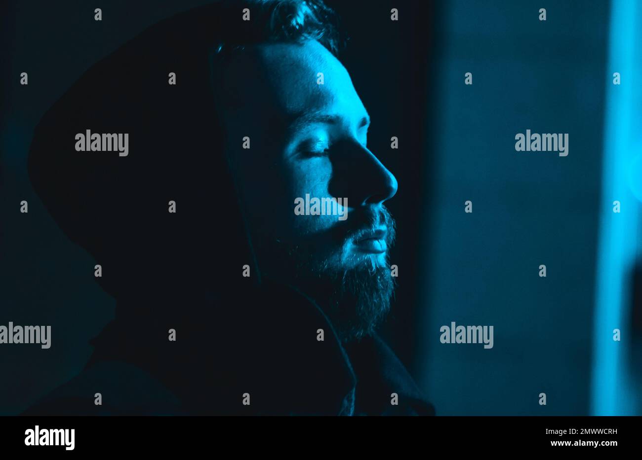 Portrait of smoking handsome man in a hood at the dark with cold blue ...