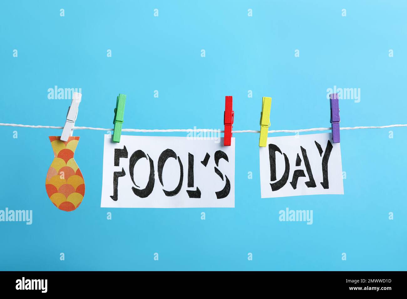 Words FOOL'S DAY and paper fish with pegs on laundry line against light ...