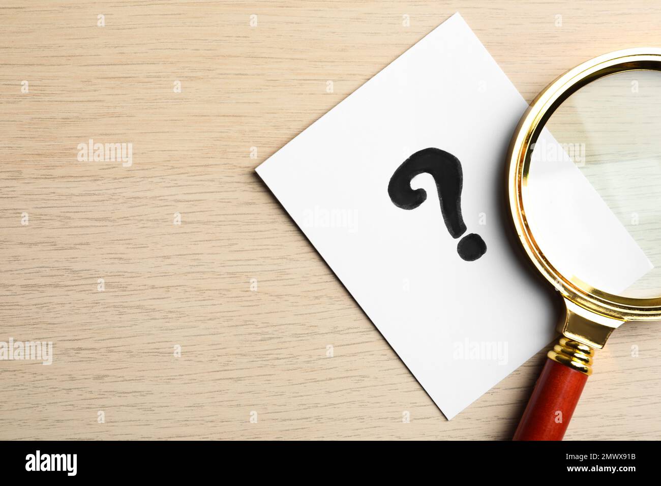 Paper card with question mark and magnifier glass on wooden table, top ...
