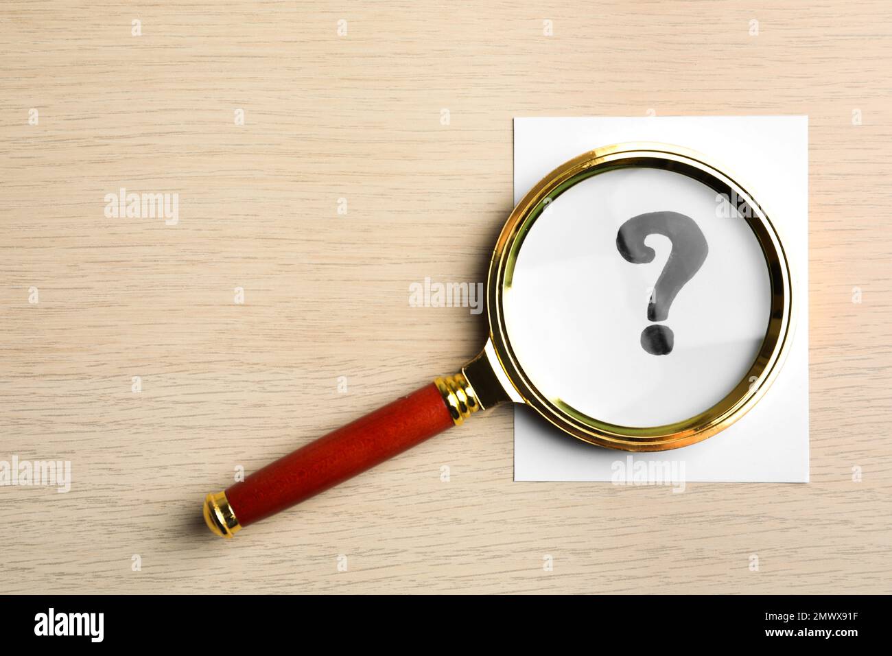 Paper card with question mark and magnifier glass on wooden table, top ...