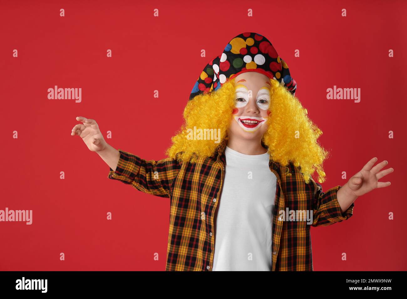 Funny little boy in clown costume on red background. April fool's day ...
