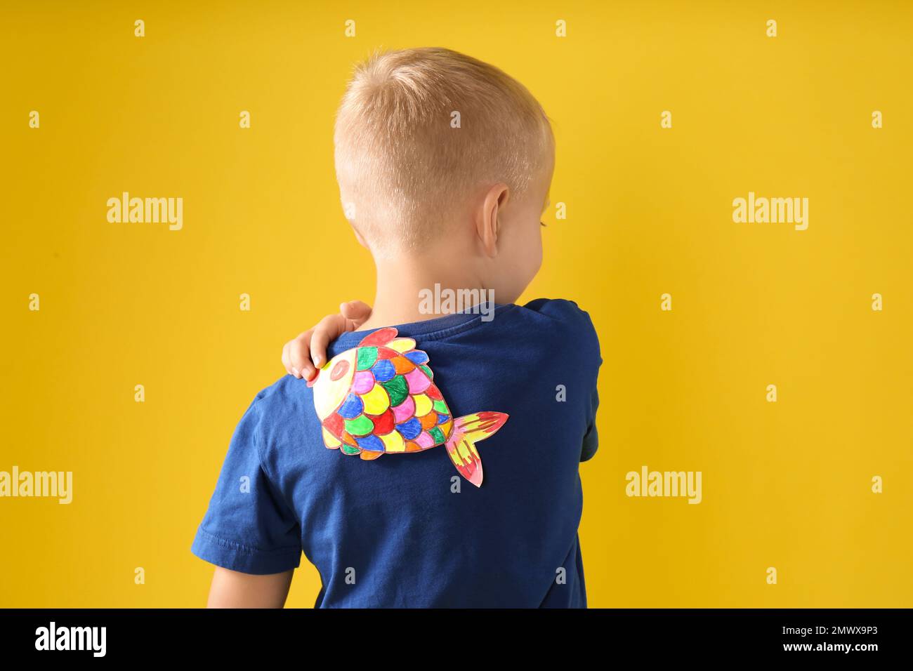 Little boy with paper fish on back against yellow background. April ...