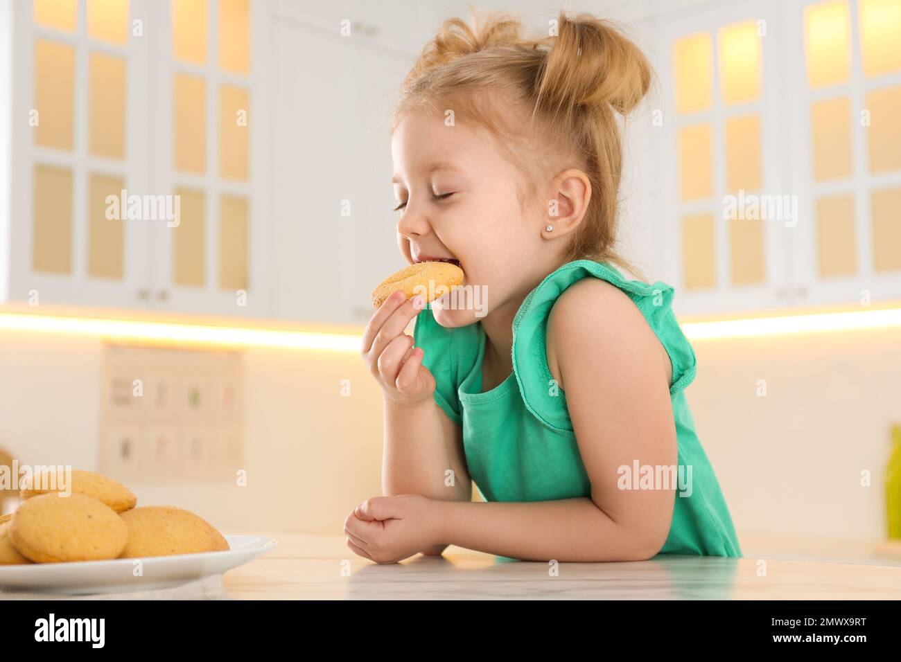 Cute little girl eating cookies in kitchen Stock Photo - Alamy