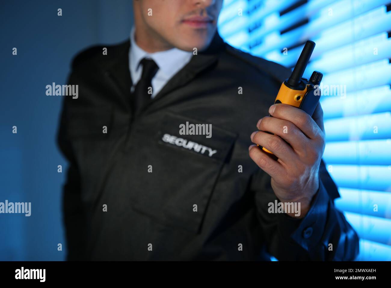 Professional security guard with portable radio set near window in dark ...