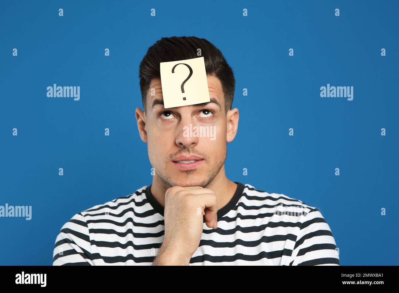 Pensive man with question mark sticker on forehead against blue ...