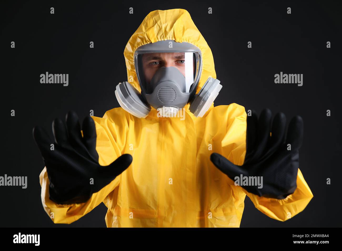 Man in chemical protective suit making stop gesture on black background ...