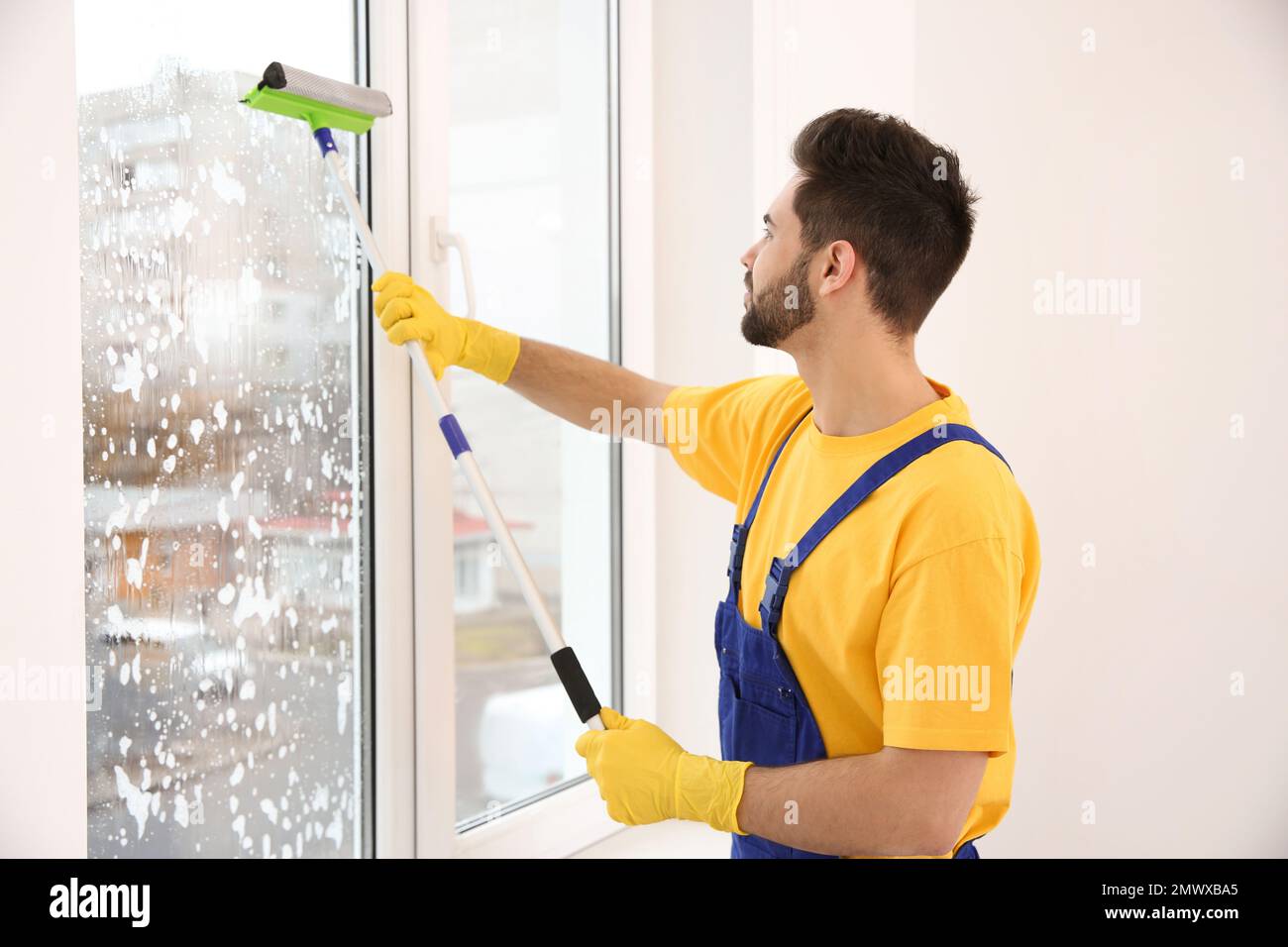 Professional young janitor in uniform cleaning window indoors Stock ...