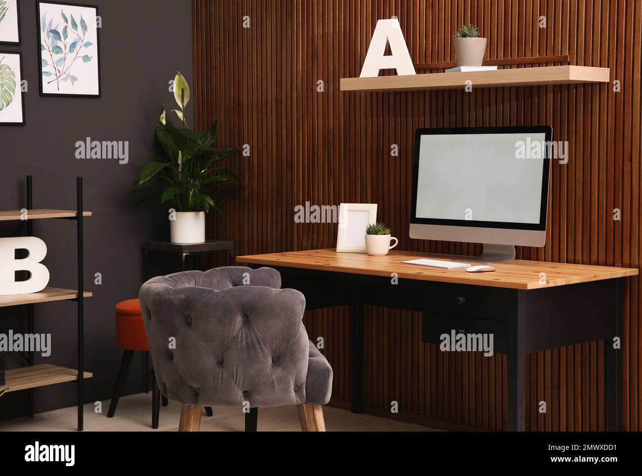 Comfortable workplace with computer near wooden wall in stylish room ...