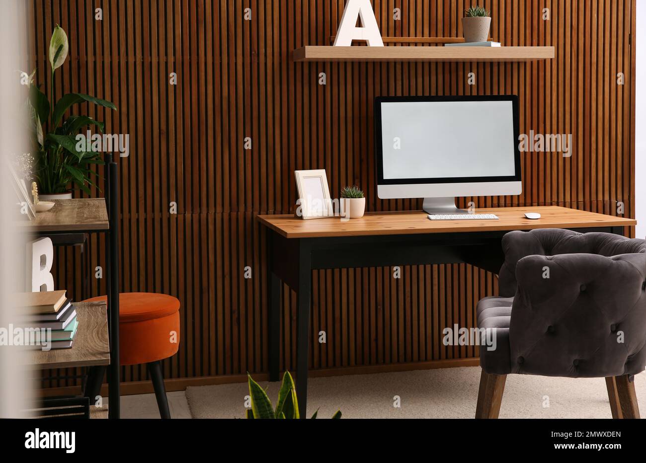 Comfortable workplace with computer near wooden wall in stylish room ...