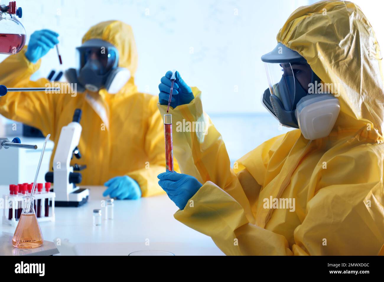 Scientist in chemical protective suit dripping blood into test tube at ...