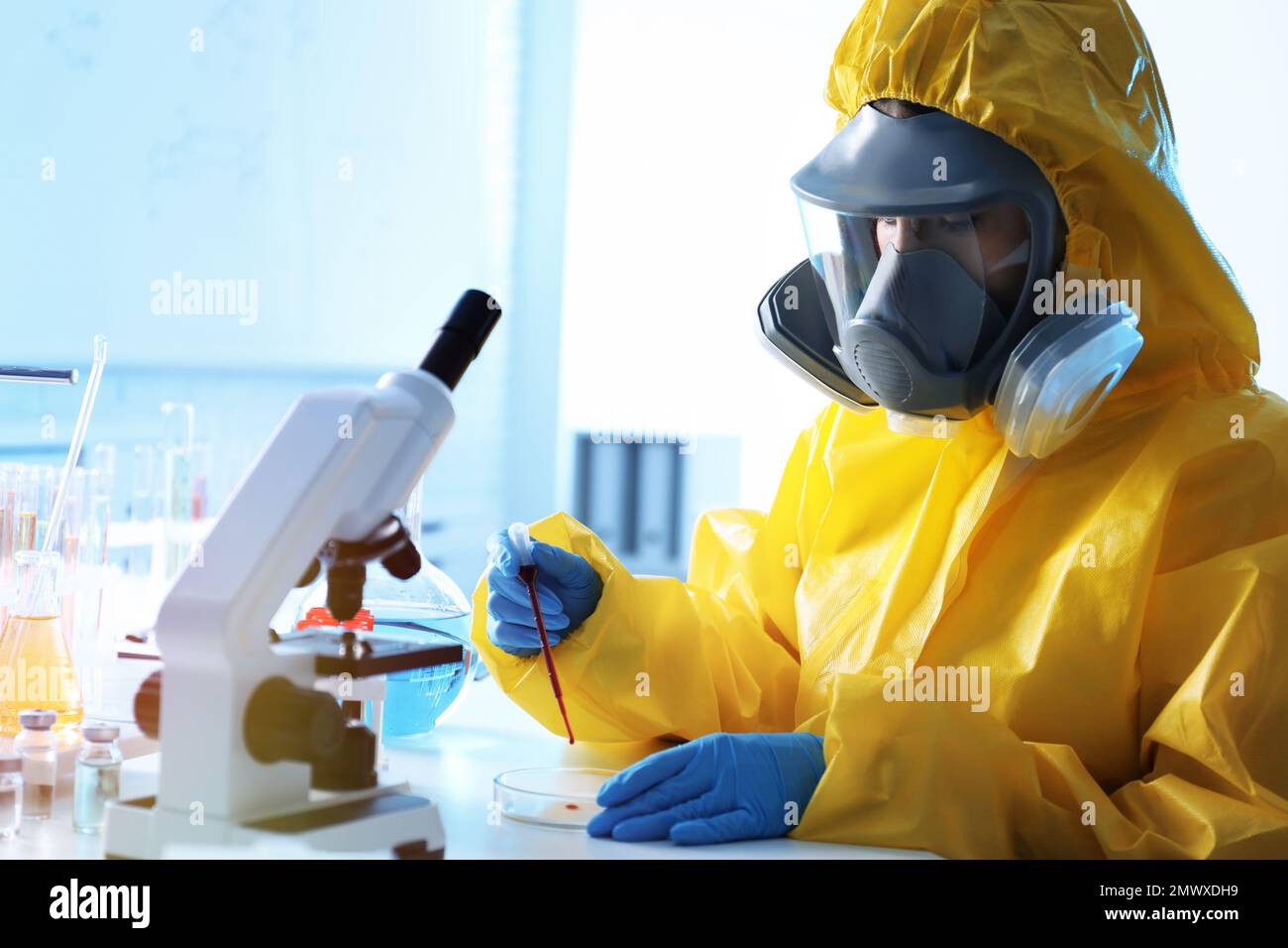 Scientist in chemical protective suit dripping blood sample into Petri ...