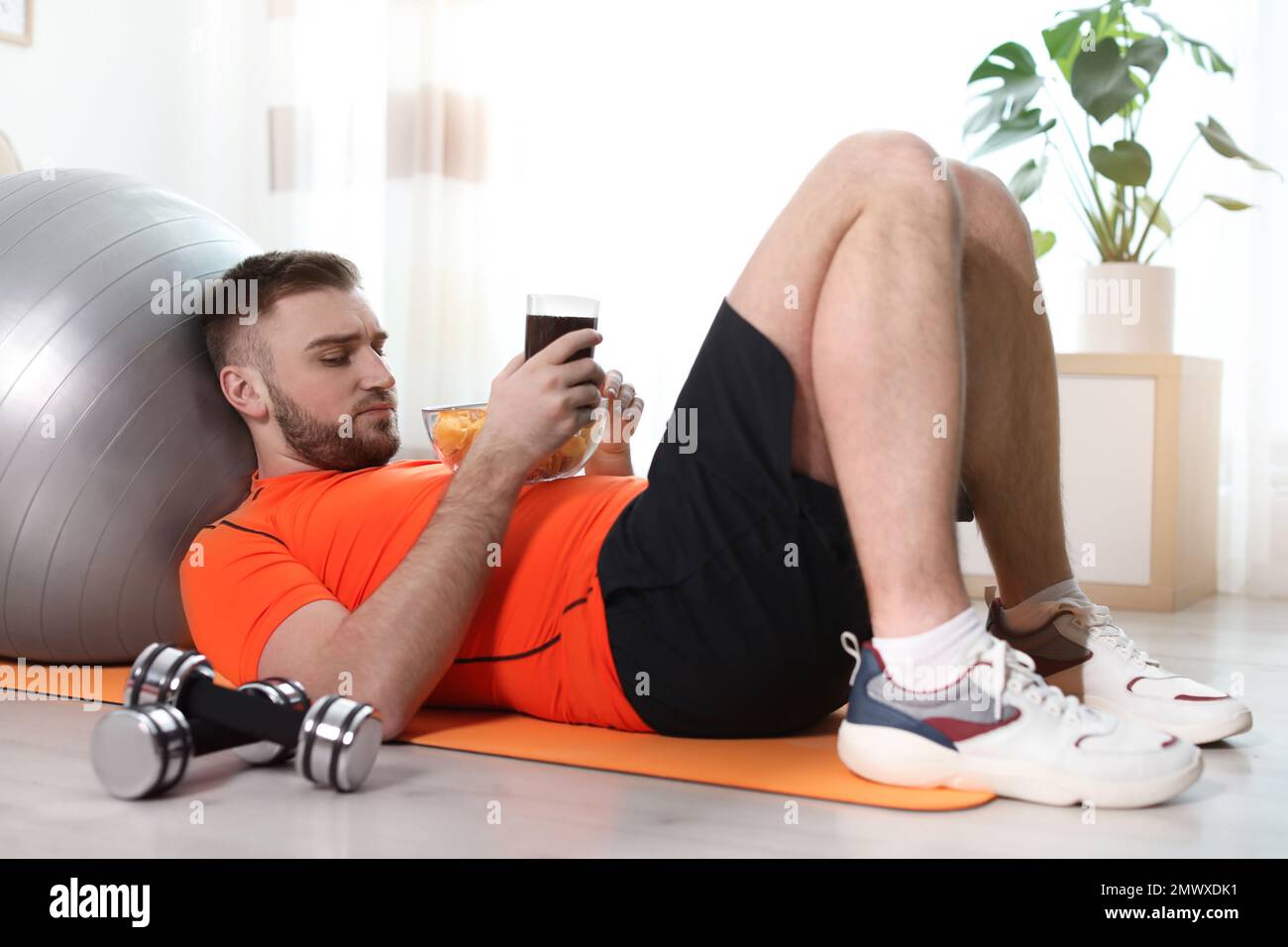 Lazy young man eating junk food on yoga mat at home Stock Photo - Alamy