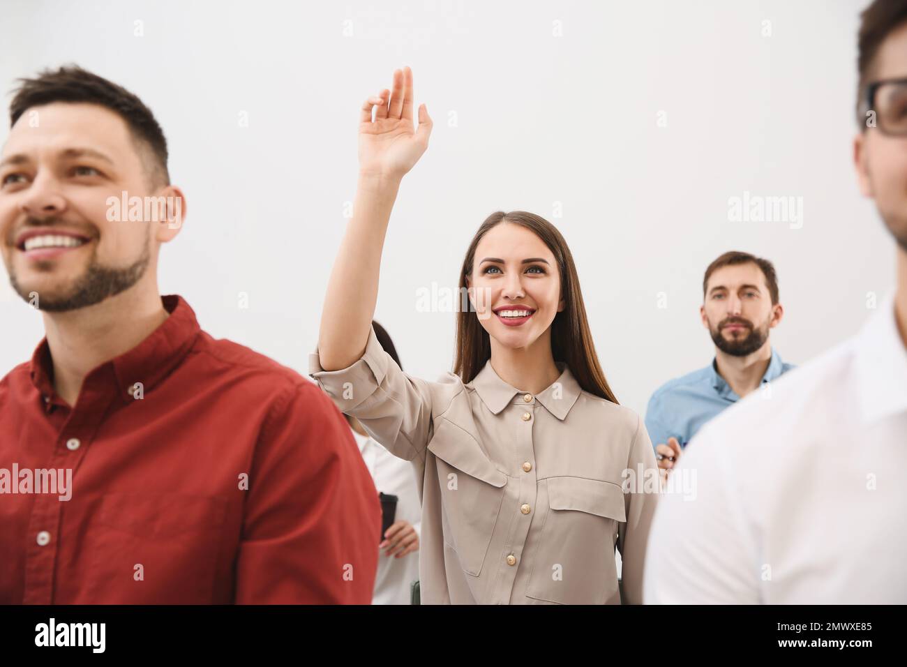 Young woman raising hand to ask question at business training on white ...