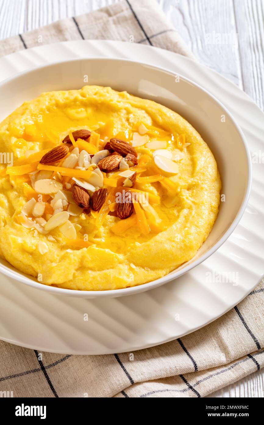 corn grits with butter, cheese, and almonds in white bowl on white wood ...