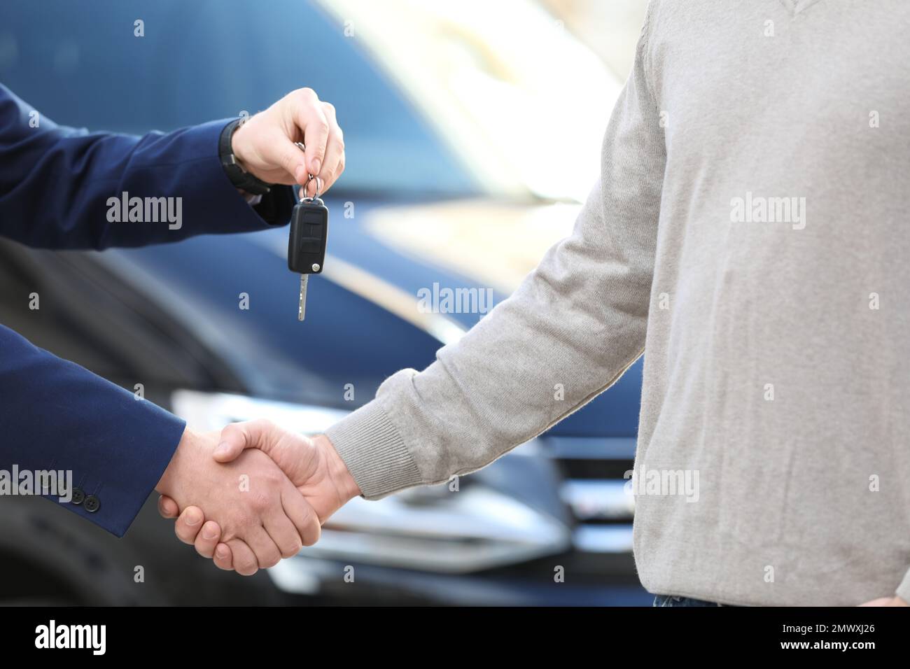 Salesman giving key to customer while shaking hands in modern auto ...