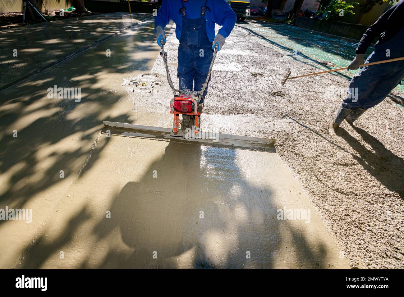 Construction worker is wearing gloves as leveling fresh concrete with ...