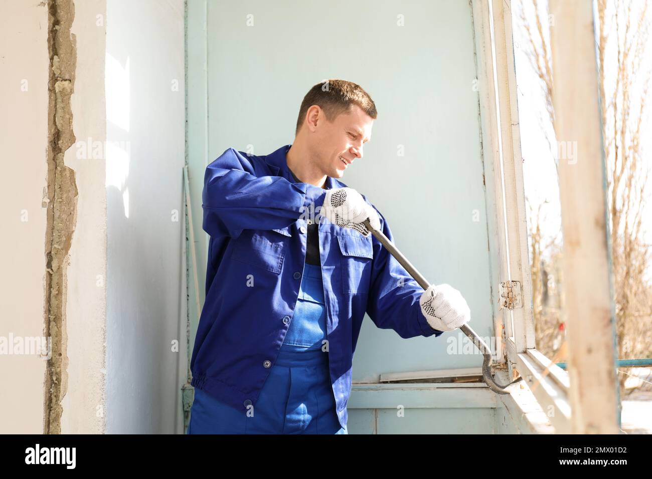 Worker dismantling old window with crowbar indoors Stock Photo - Alamy