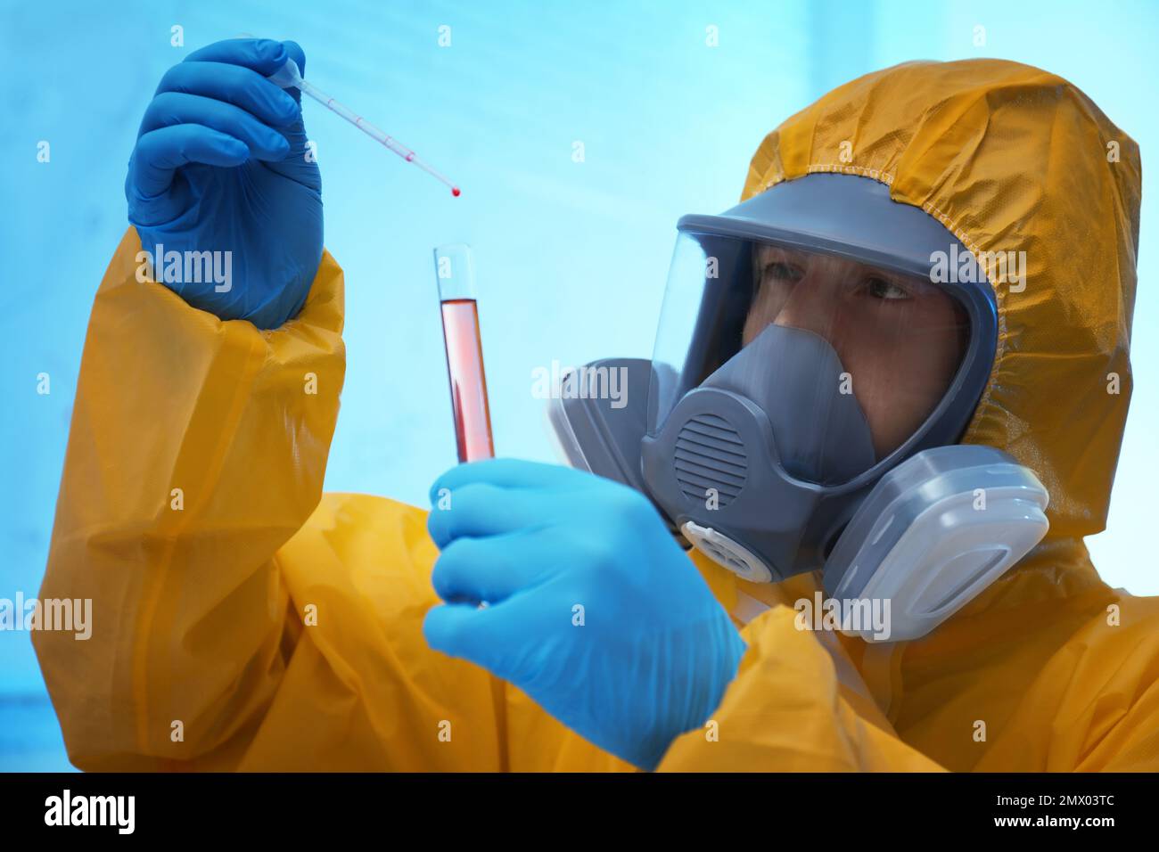 Scientist in chemical protective suit dripping reagent into test tube ...