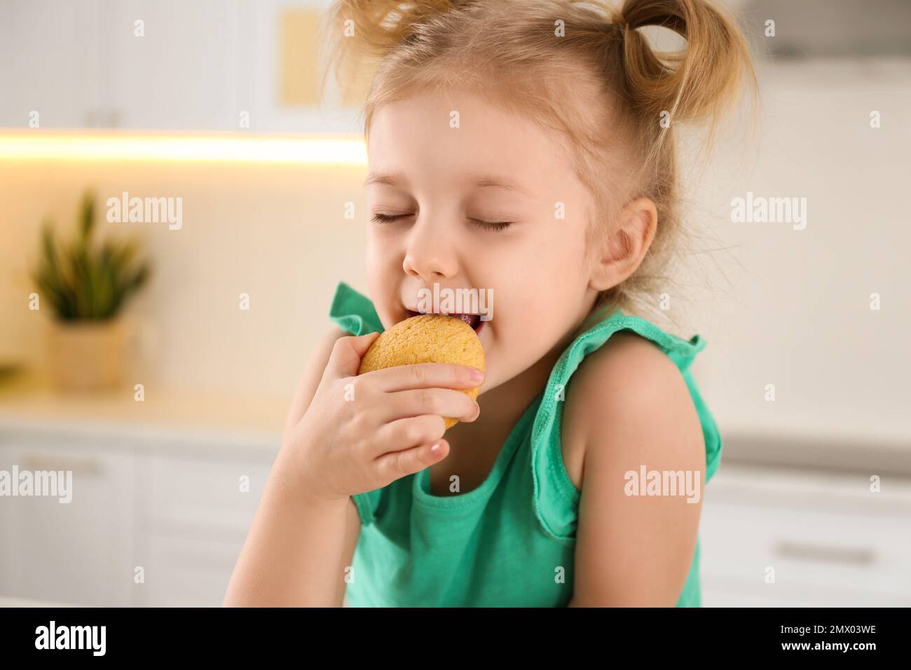 Cute little girl eating cookies in kitchen Stock Photo - Alamy