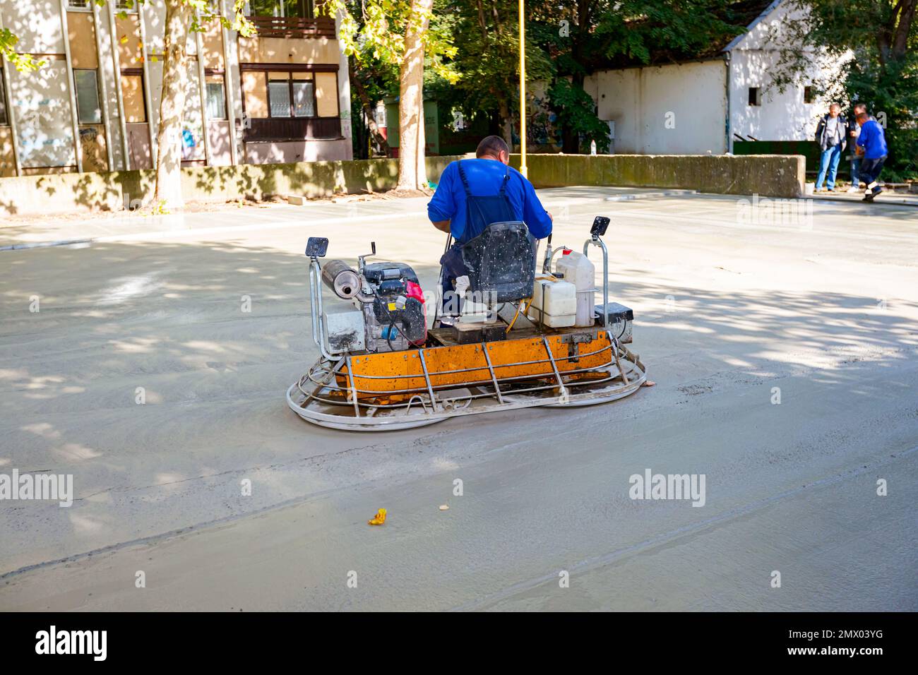 Worker sitting on a self-leveling power trowel machine with gas engine ...