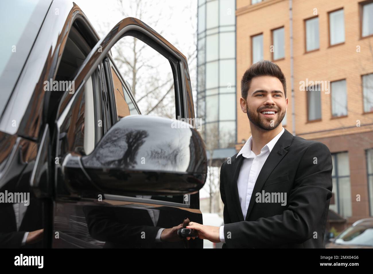 Handsome young man opening door of modern car outdoors Stock Photo - Alamy