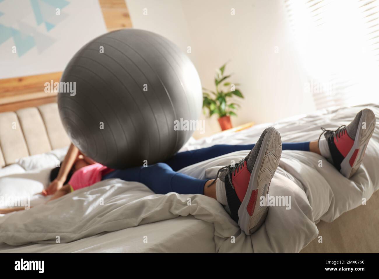 Lazy young woman with exercise ball sleeping on bed, focus on legs ...