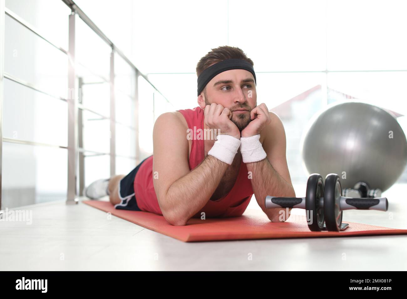 Lazy young man with abs roller lying on yoga mat indoors Stock Photo ...